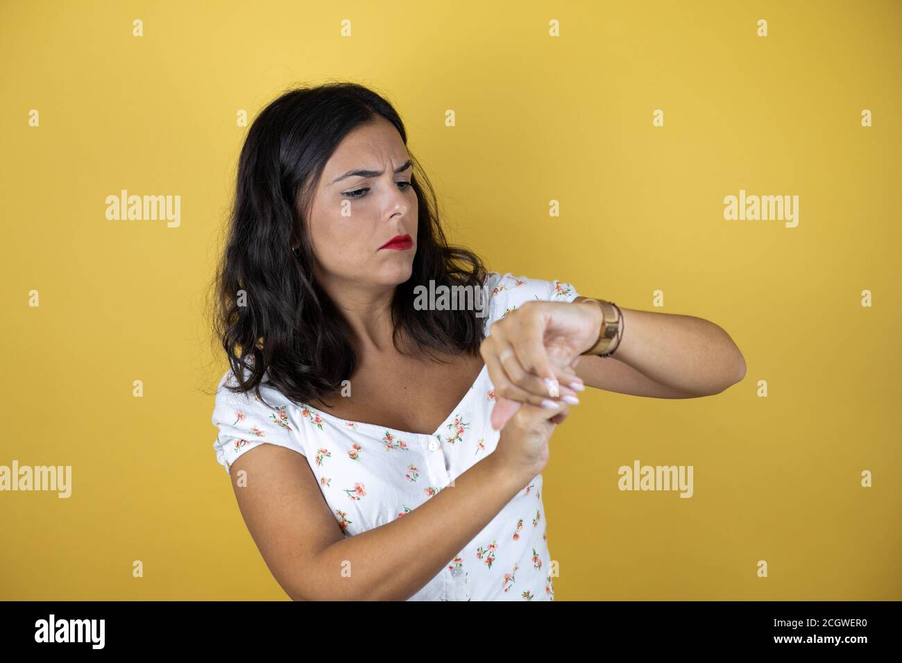 Beautiful woman over yellow background surprised and pointing his watch ...