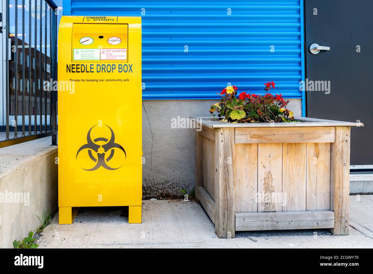 A public drop box for used needles, on a sidewalk by a building. The ...