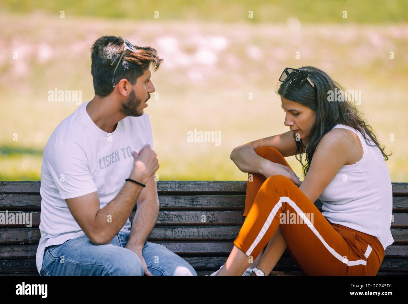 Happy casual couple talking looking each other sitting in a park with a ...