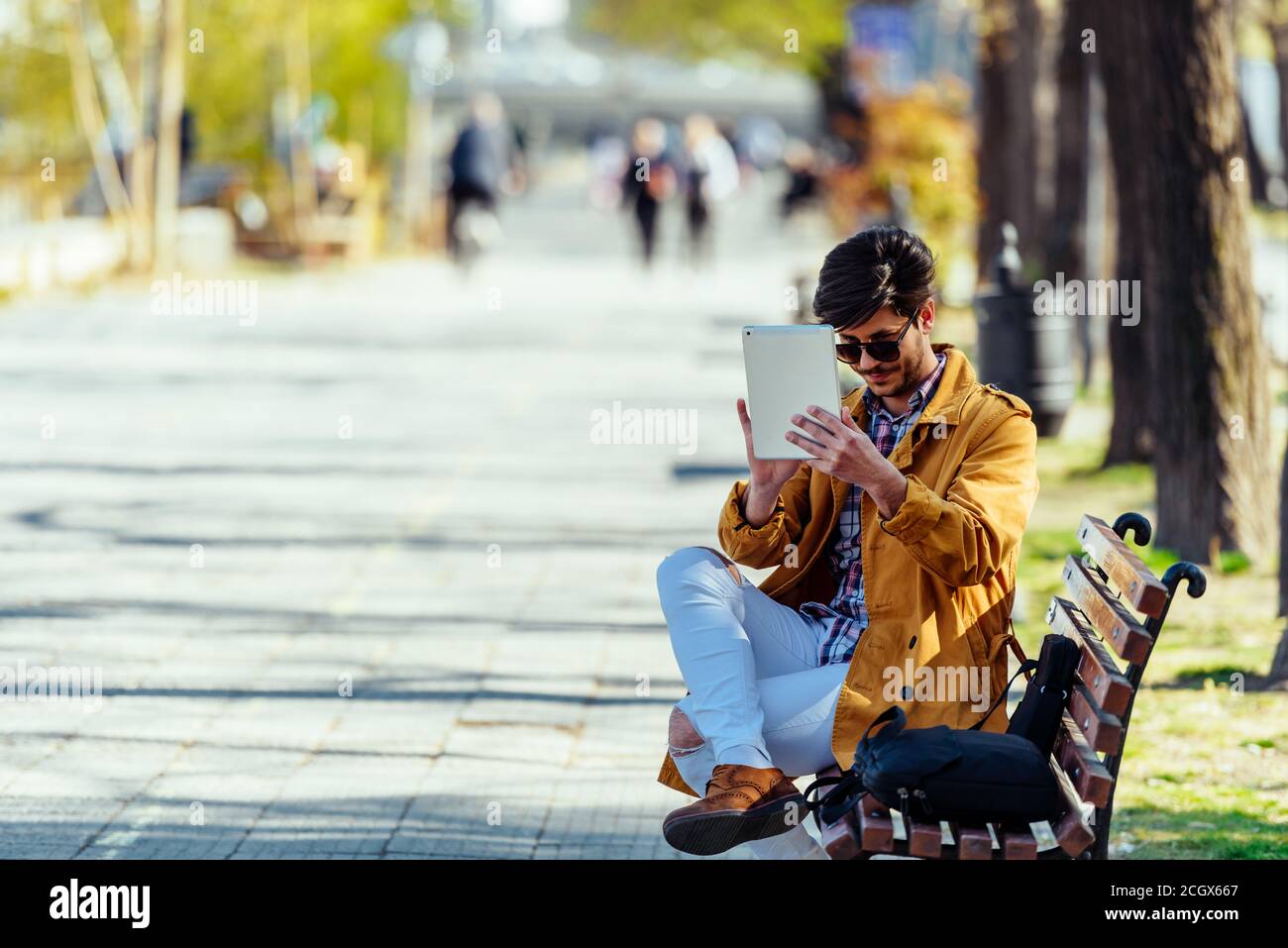 Modern guy sitting on bench in the park and making photo with his ...