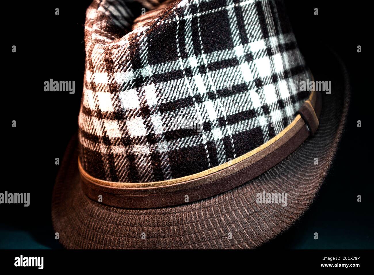 Detail view of checkered fedora with tri color leather band in darkness ...