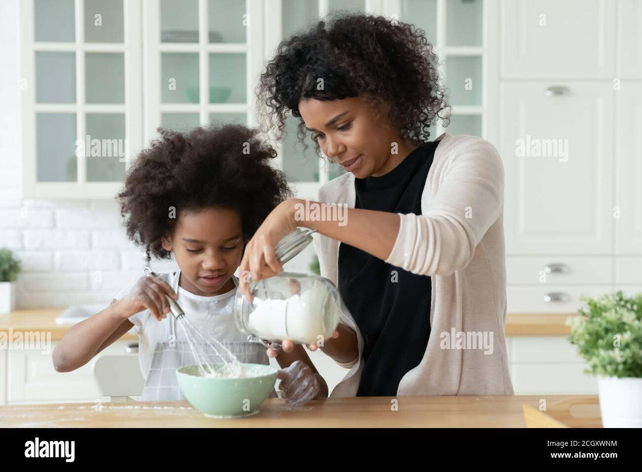 Caring young african american mother helping little daughter with ... Caring young african american mother helping little daughter with ...