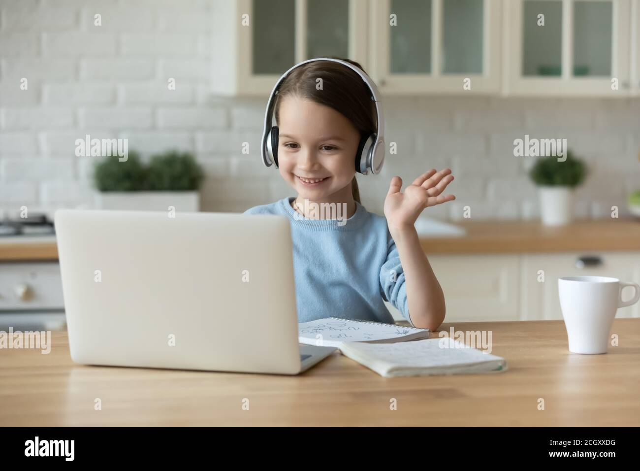 Little girl in headphones looking at computer screen, waving hello ...