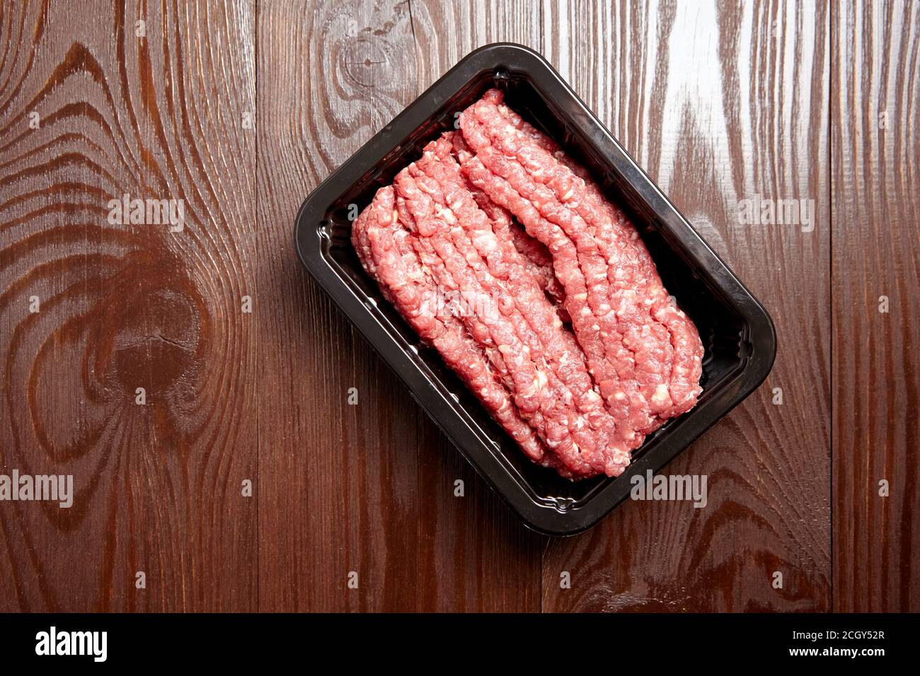 Ground beef in a black plastic tray on wooden table, top view with copy ...