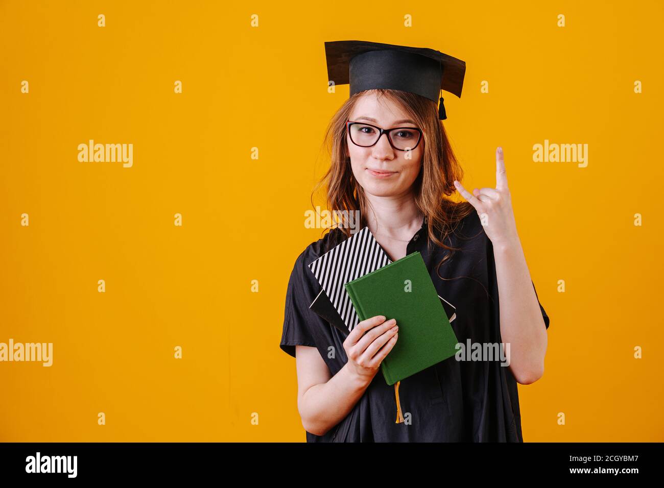 Woman celebrating her graduation, wearing gown and hat. Over orange ...