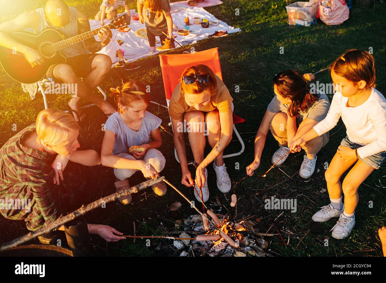 Friends and family gathered around bonfire, having picnic. On a spring ...