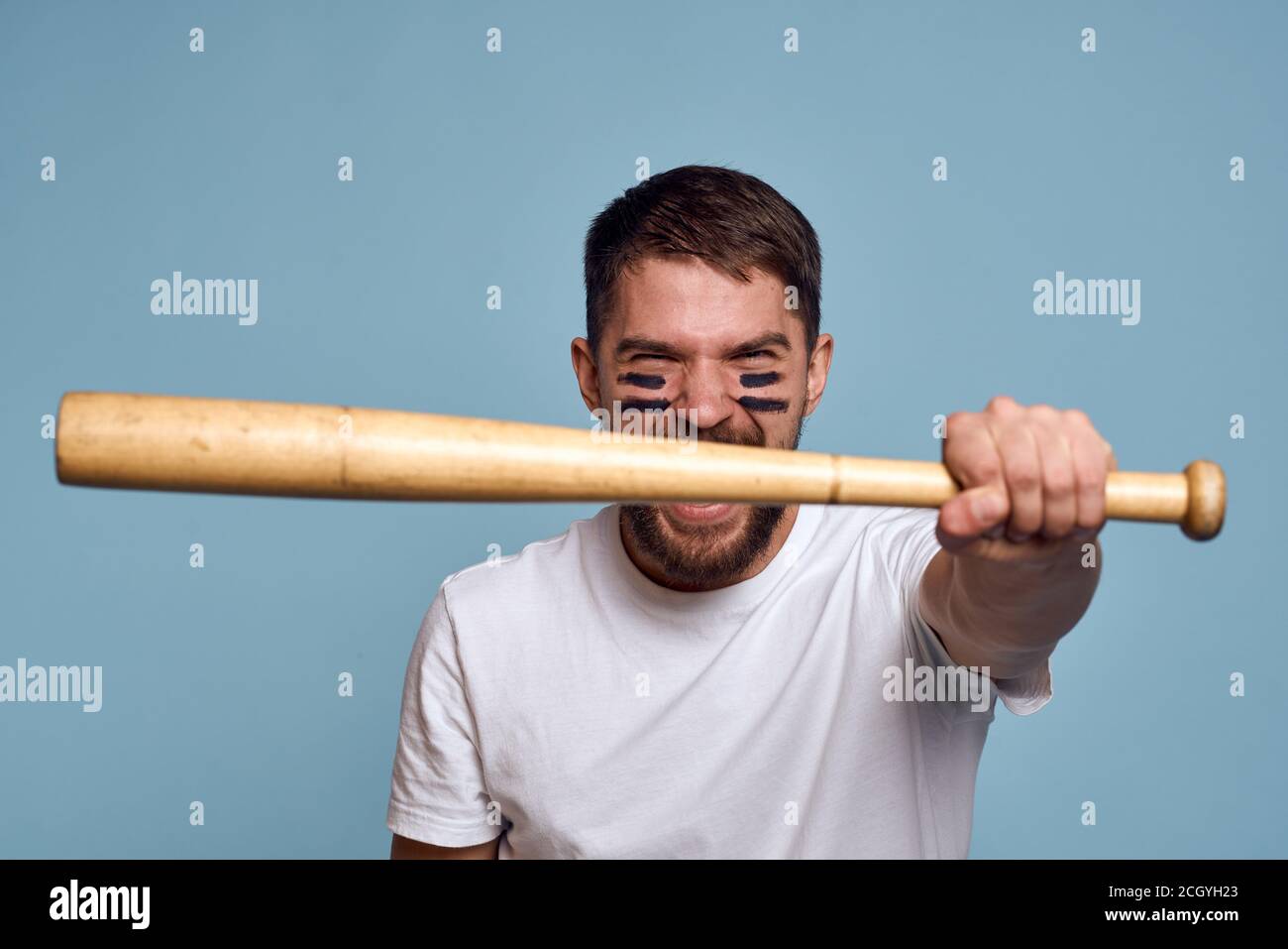 emotional man with a bat in his hand on a blue background and makeup on ...