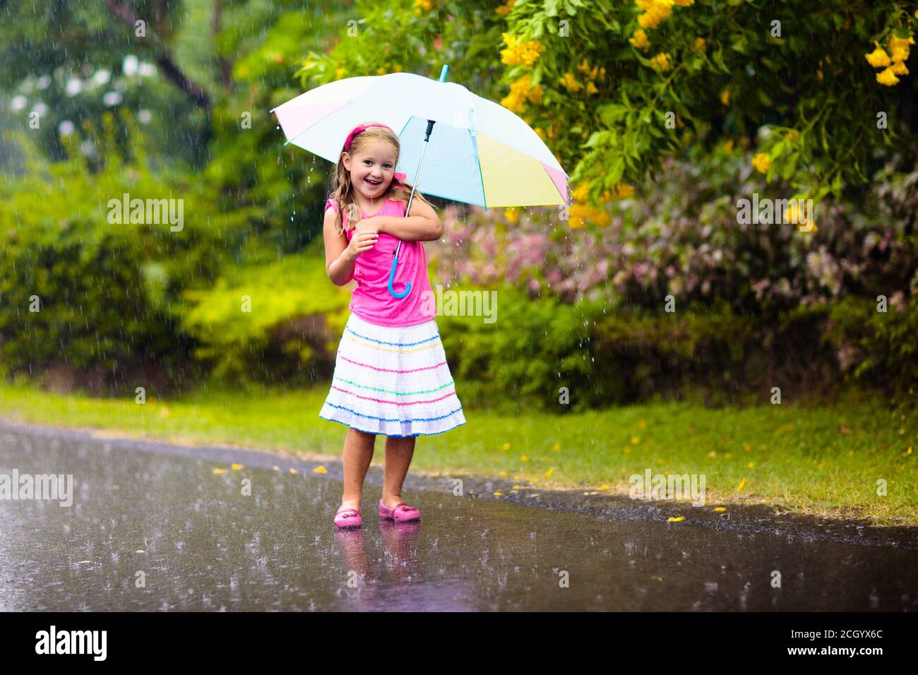Kid playing out in the rain. Children with umbrella play outdoors in ...