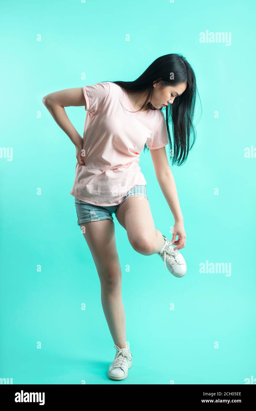 Asian sporty woman with long hair in denim shorts adjusting laces on ...