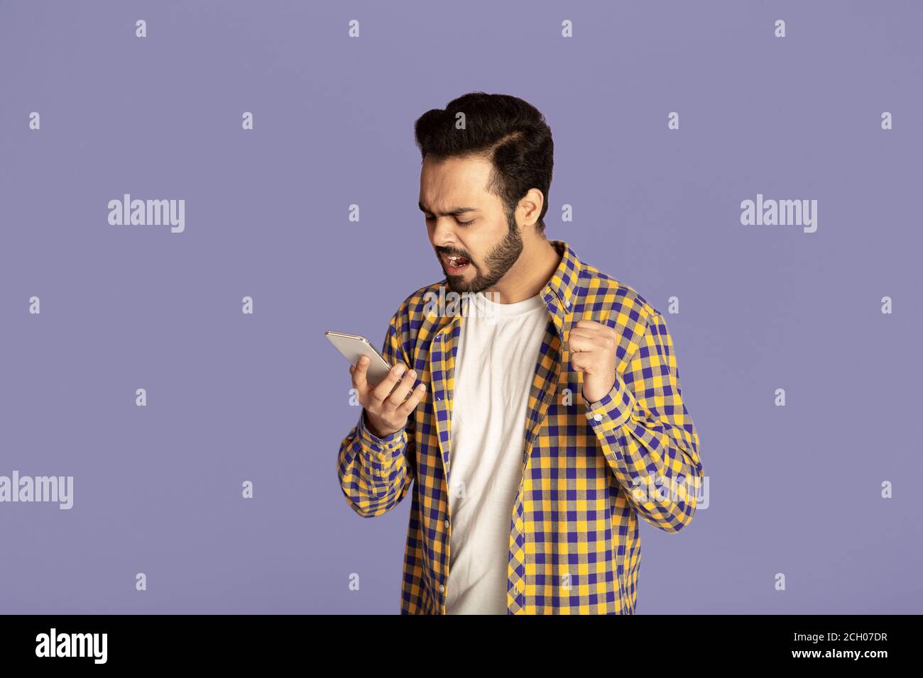 Angry Indian man screaming at his smartphone over lilac background ...