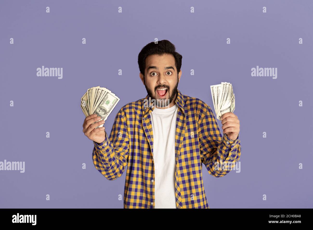 Shocked Indian man with hands full of money shouting WOW on lilac ...