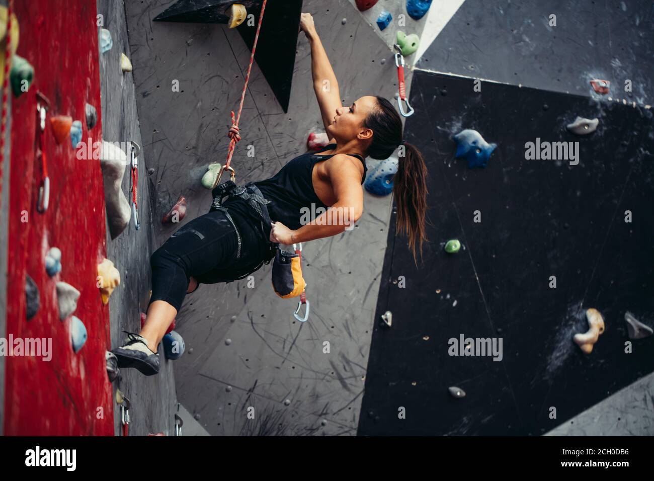 Woman climber reaching the top of steep artificial wall. Hanging on air ...