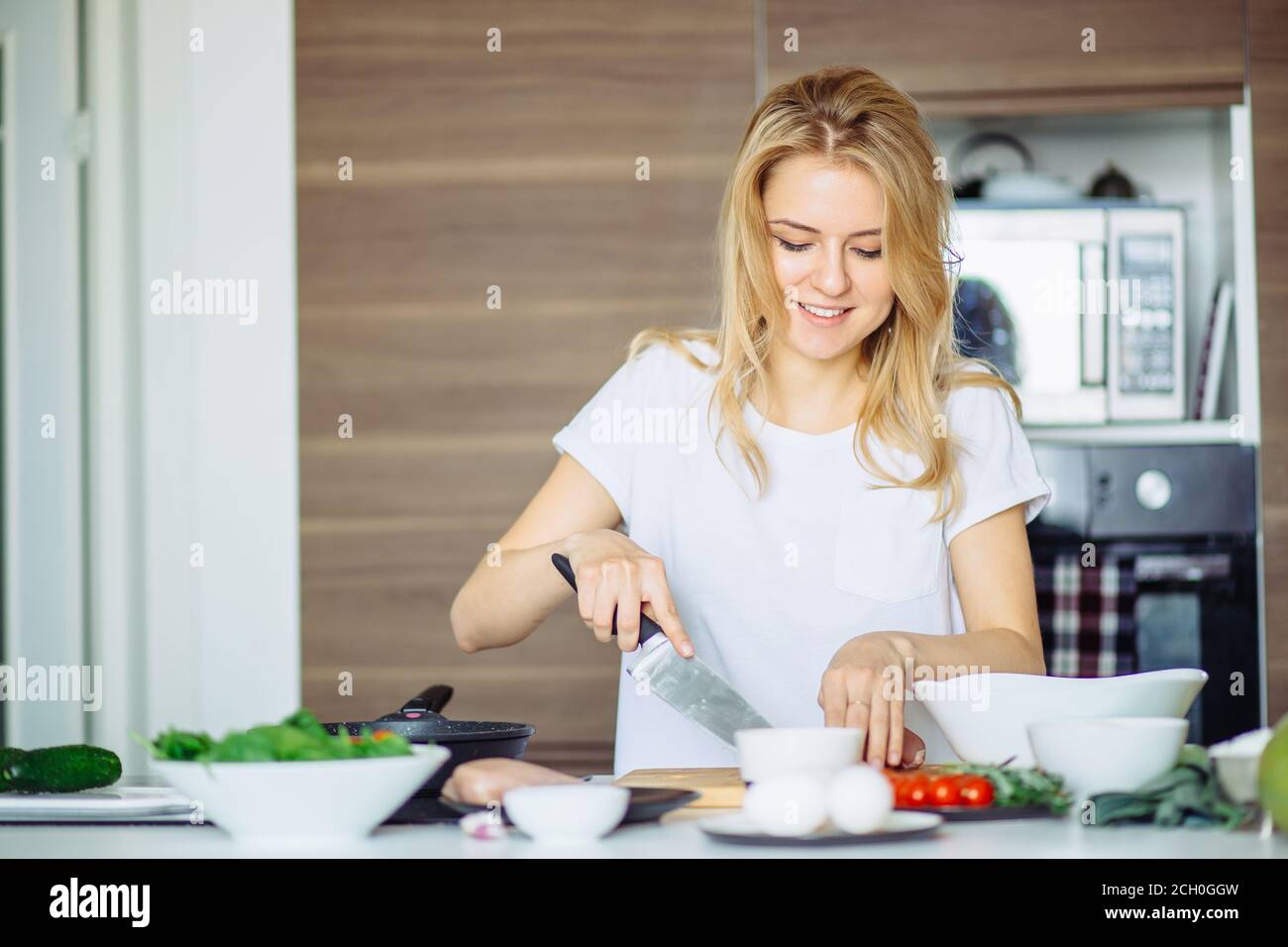 Woman cutting chicken meat on a kitchen table with a big Chef knife on ...