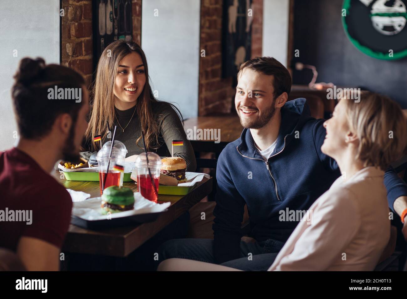 Group of joyful young students sitting in street bar , snacking by ...