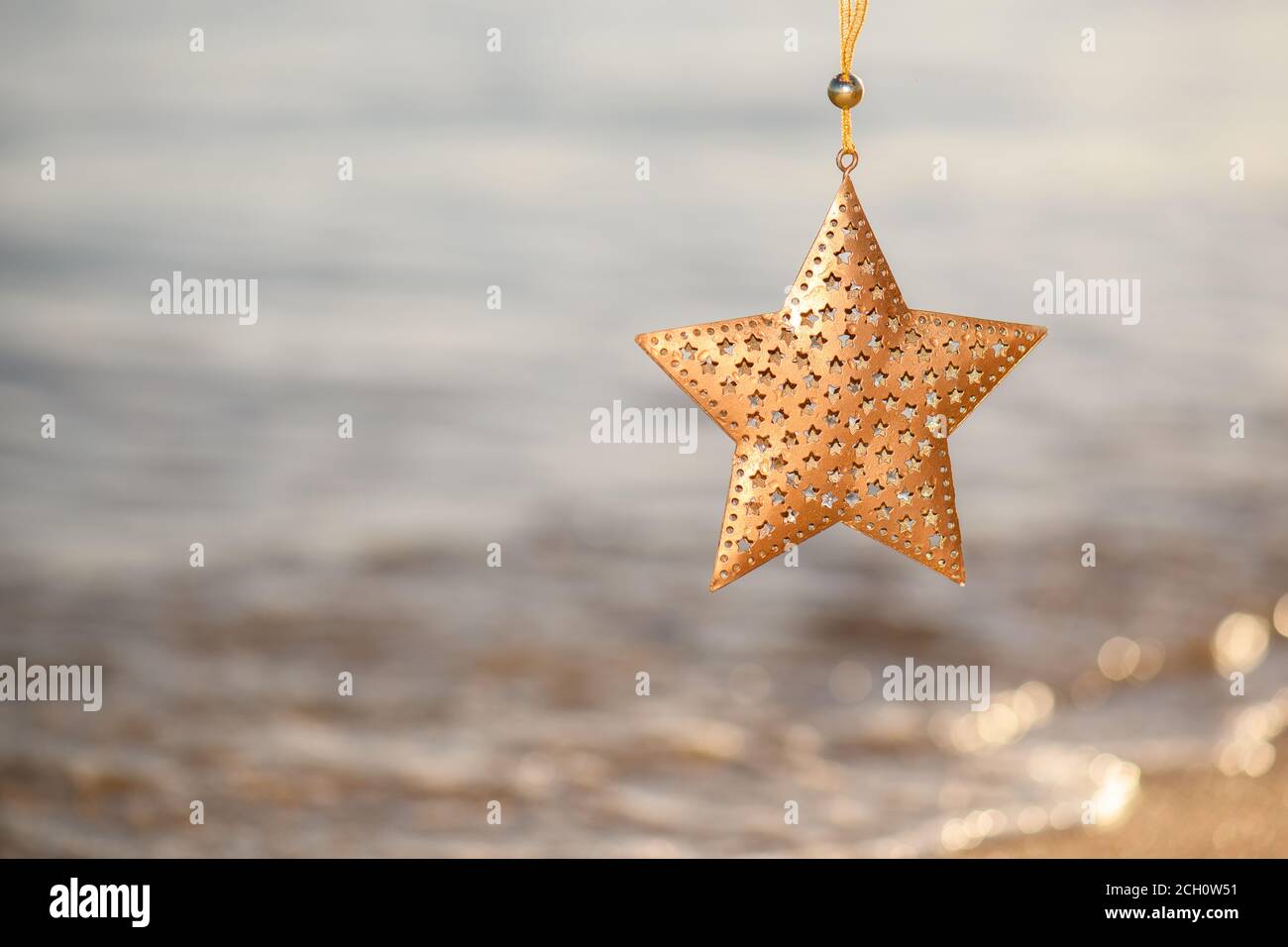 Christmas gold star decoration on the beach near the wave on ocean or ...