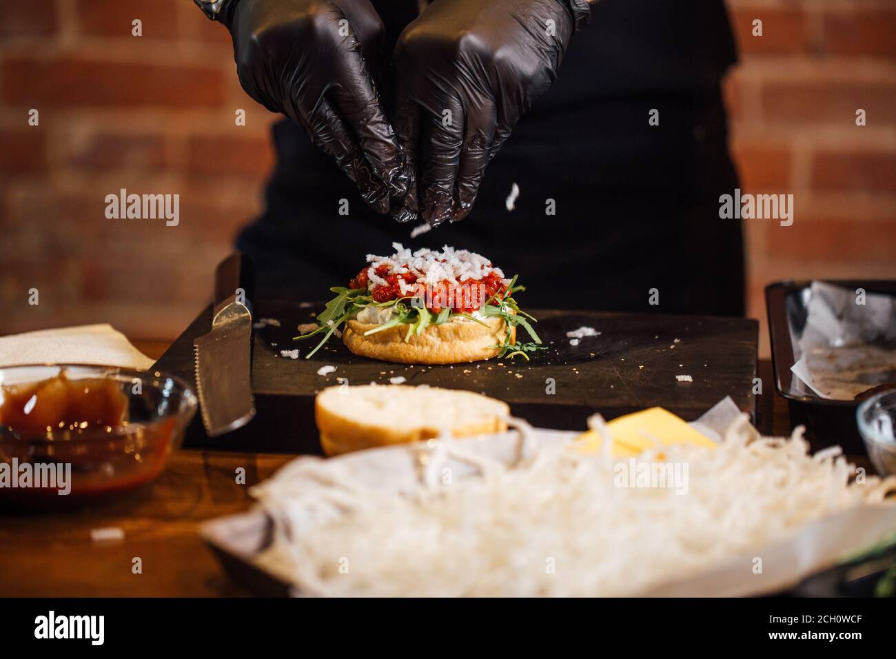 Close up of appetising beef burger. Chef hands pouring cheese on half ...