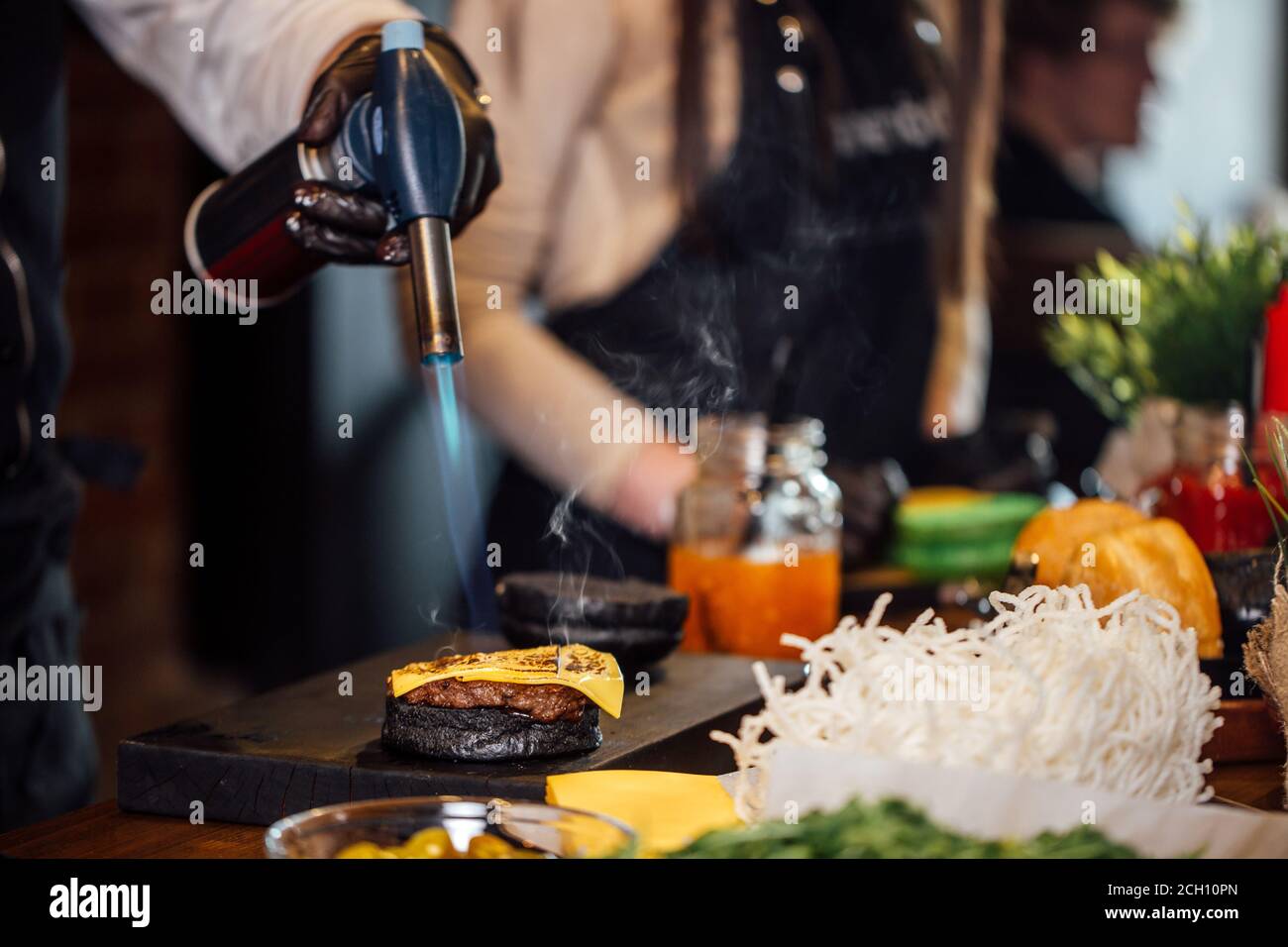 Chef taking part in BurgerChef Competition burning cheese on burger bun ...