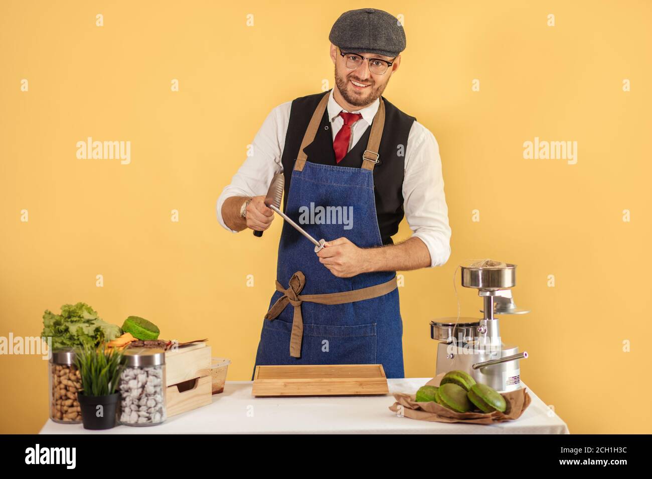 Portrait of chef cook in elegant uniform wearing cap and apron sharpens ...