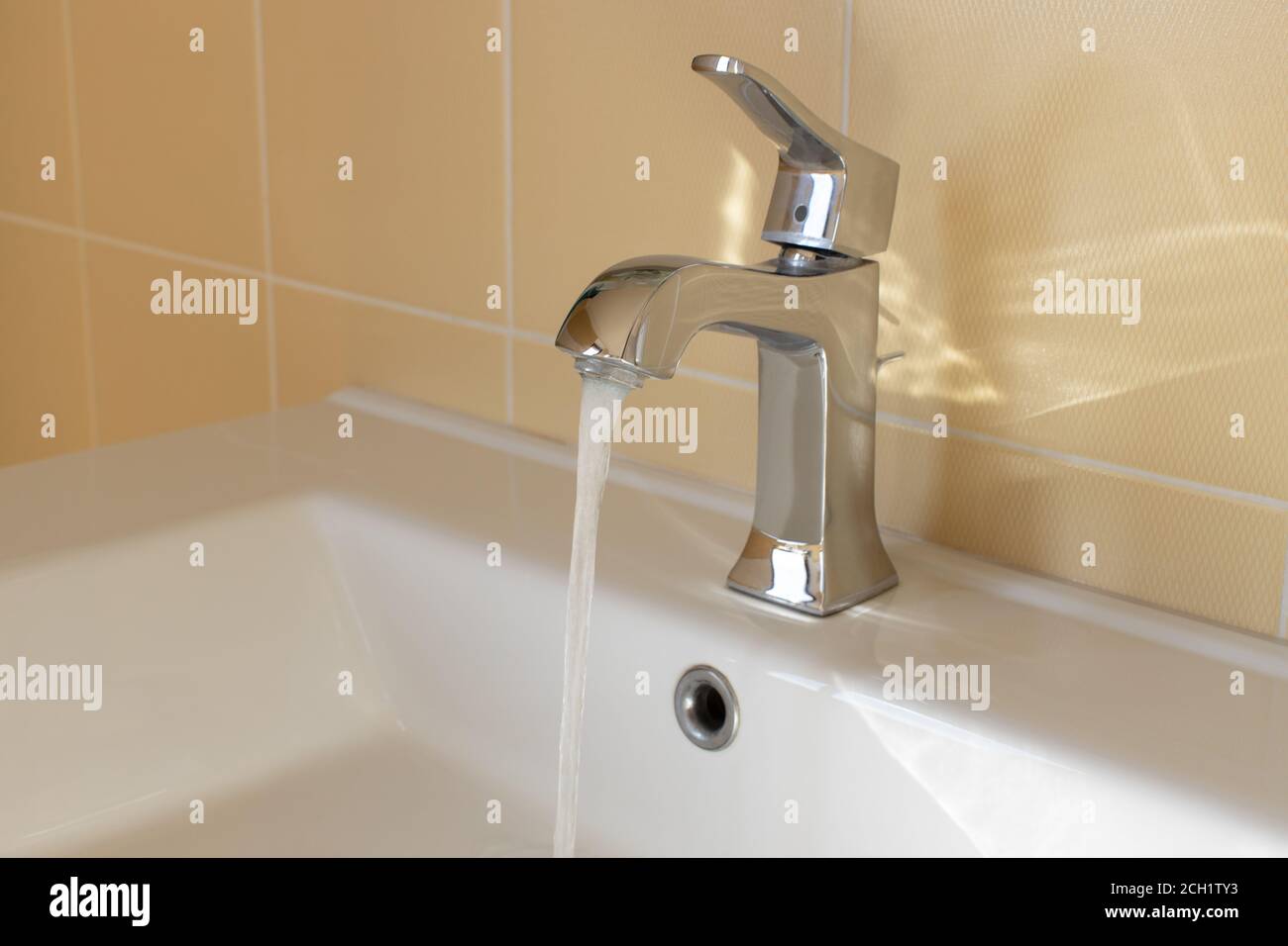 Modern faucet in yellow bathroom with running water, close up, side ...