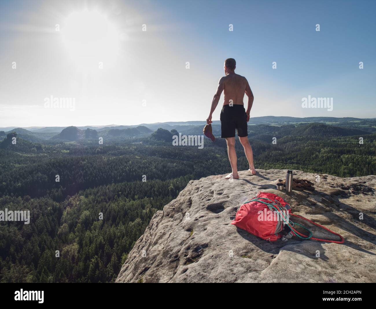 Muscular shirtless man have lunch in rocks. Hiker with heavy backpack ...