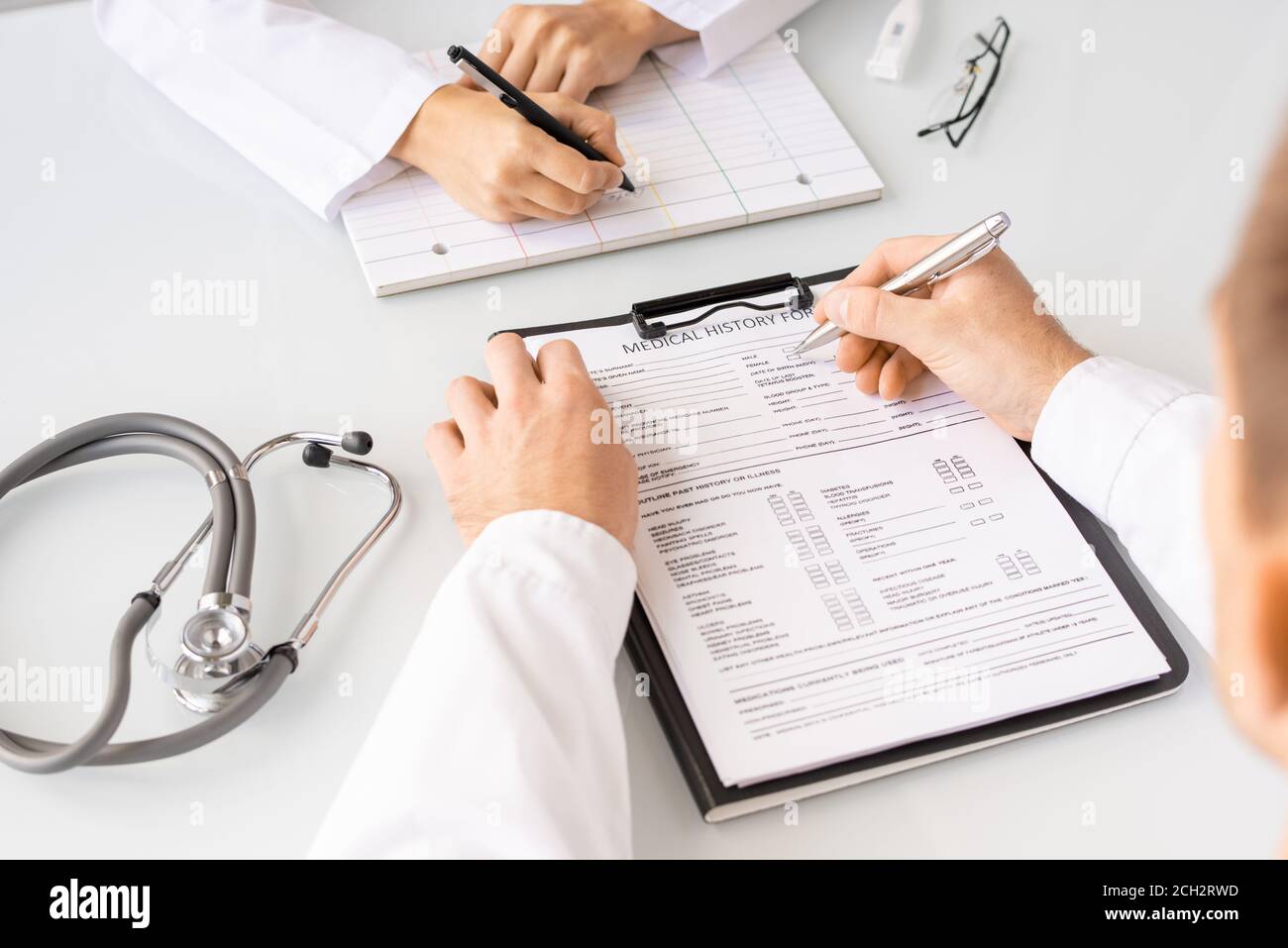 Hands of young doctor with pen filling in medical history forms of ...