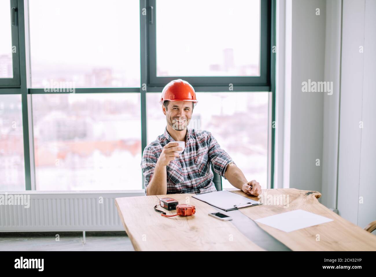 positive construction worker drinking coffee at work. panorama window ...