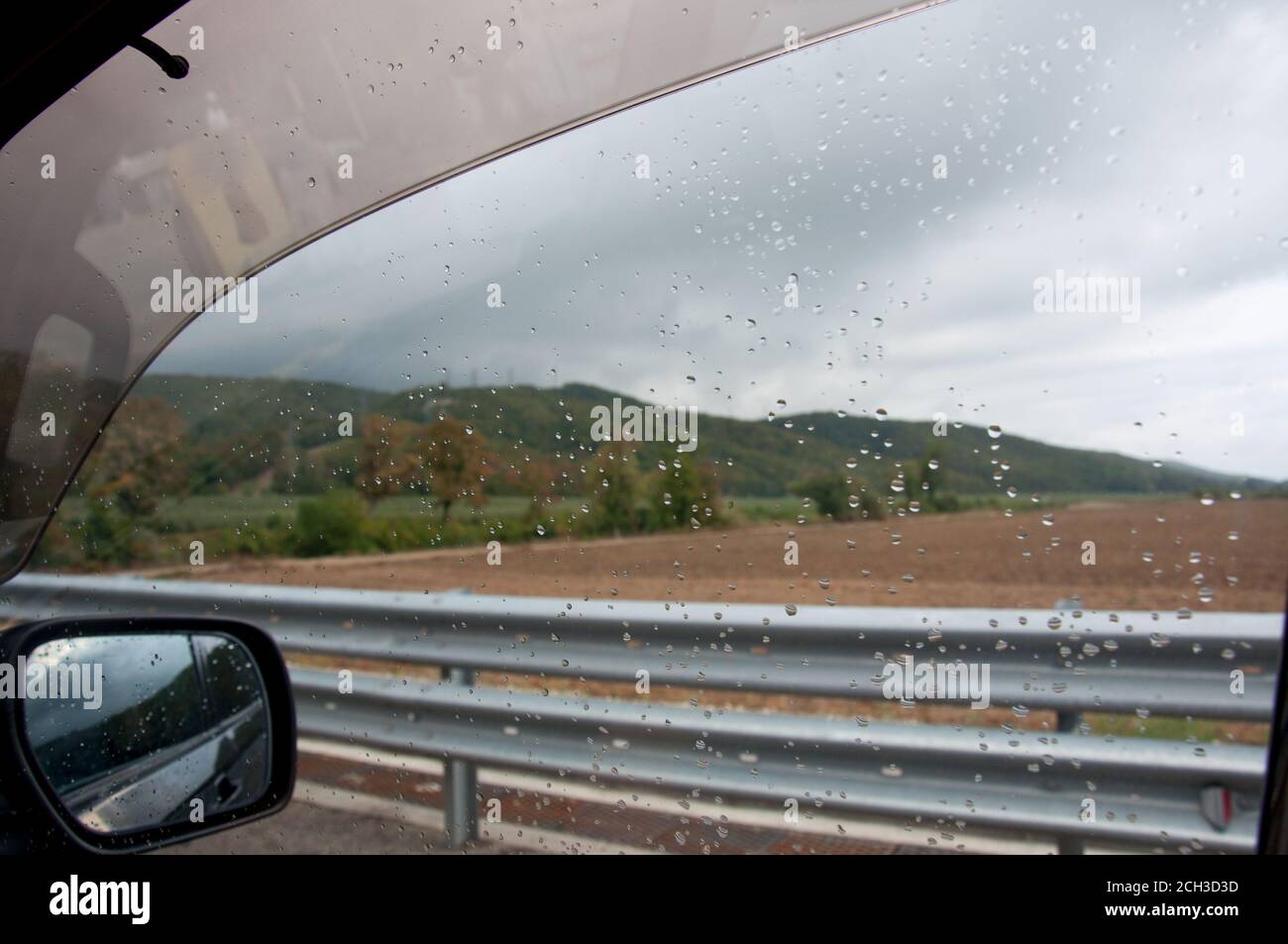 Raindrops on car glass during the day. Cloudy weather outside the car ...
