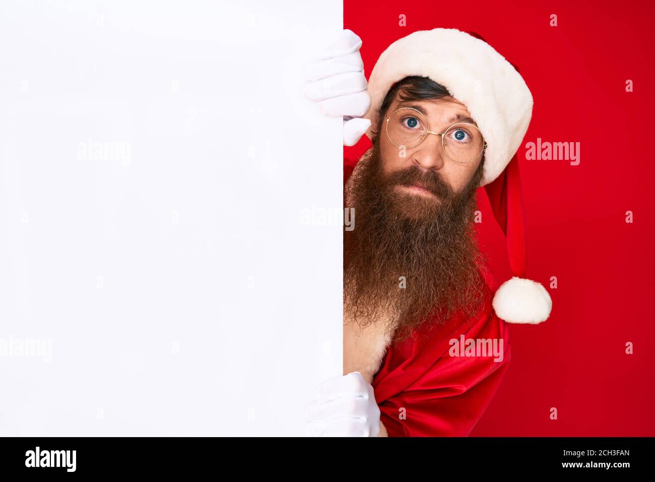 Handsome young red head man with long beard wearing santa claus costume ...