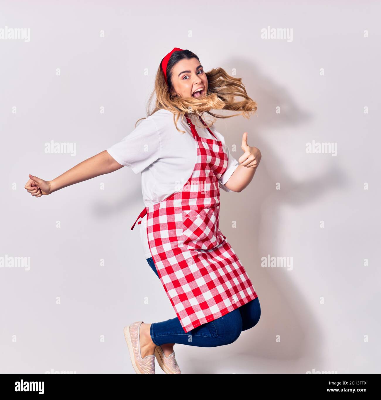 Young beautiful blonde cook woman wearing apron smiling happy. Jumping ...