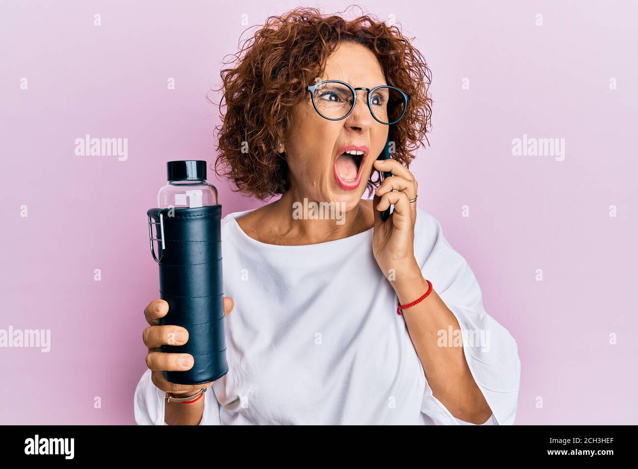 Beautiful middle age mature woman using smartphone holding water bottle ...