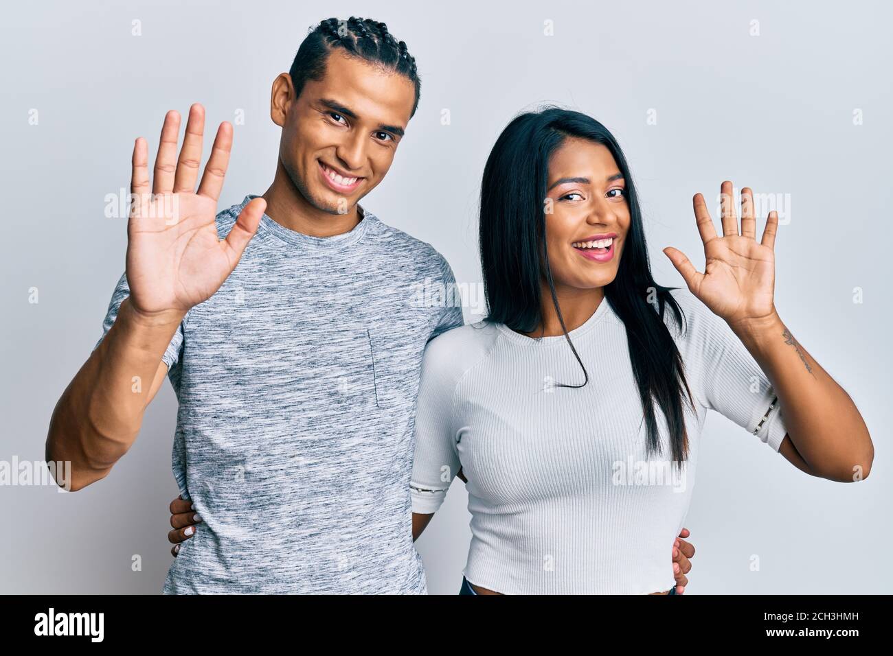 Young latin couple wearing casual clothes waiving saying hello happy ...