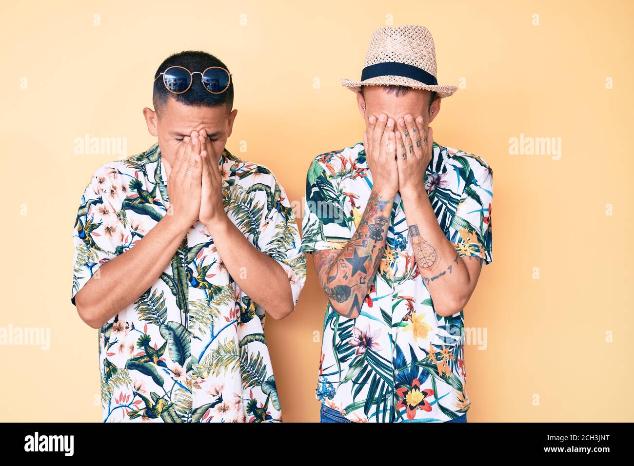 Young gay couple of two men wearing summer hat and hawaiian shirt with ...