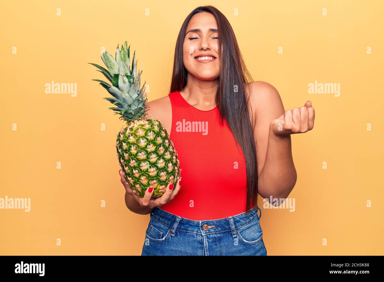 Young beautiful brunette woman holding pineapple screaming proud ...