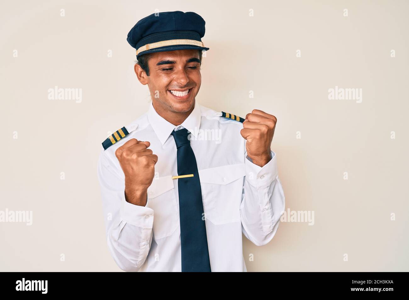 Young hispanic man wearing airplane pilot uniform celebrating surprised ...