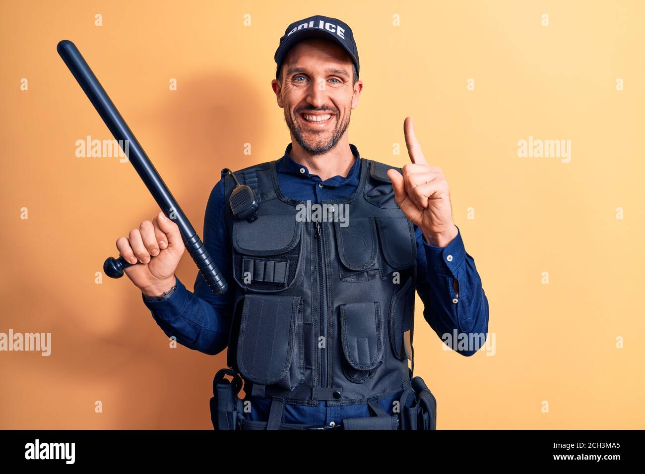 Handsome policeman wearing uniform and bulletprof holding baton over ...