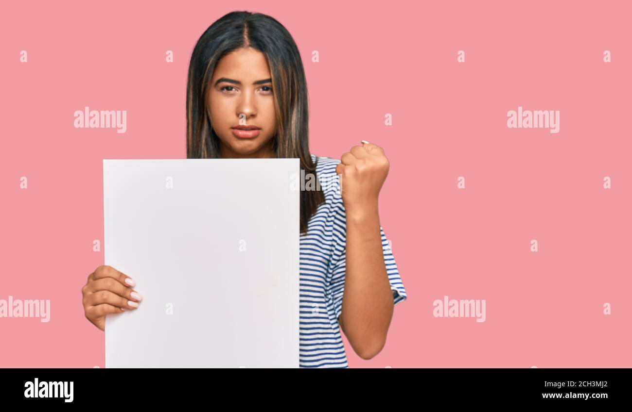 Young latin girl holding blank empty banner annoyed and frustrated ...