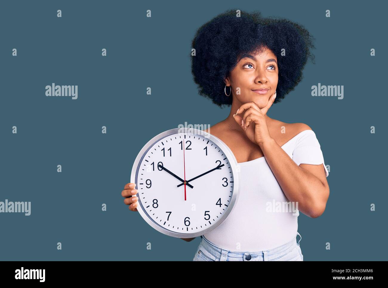 Young african american girl holding big clock serious face thinking ...