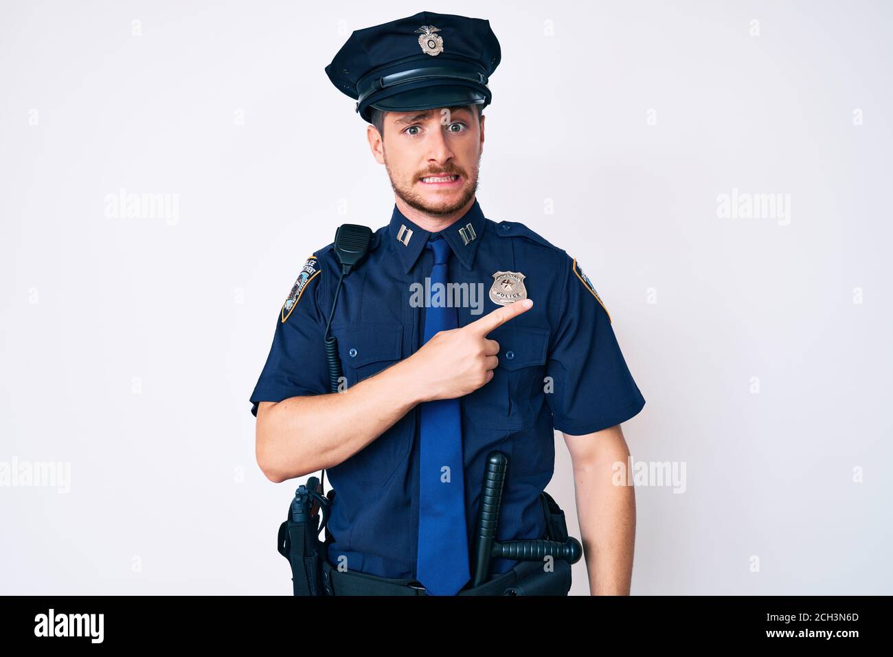 Young caucasian man wearing police uniform pointing aside worried and ...
