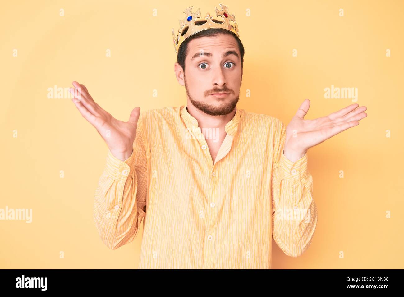 Young handsome man wearing king crown clueless and confused with open ...