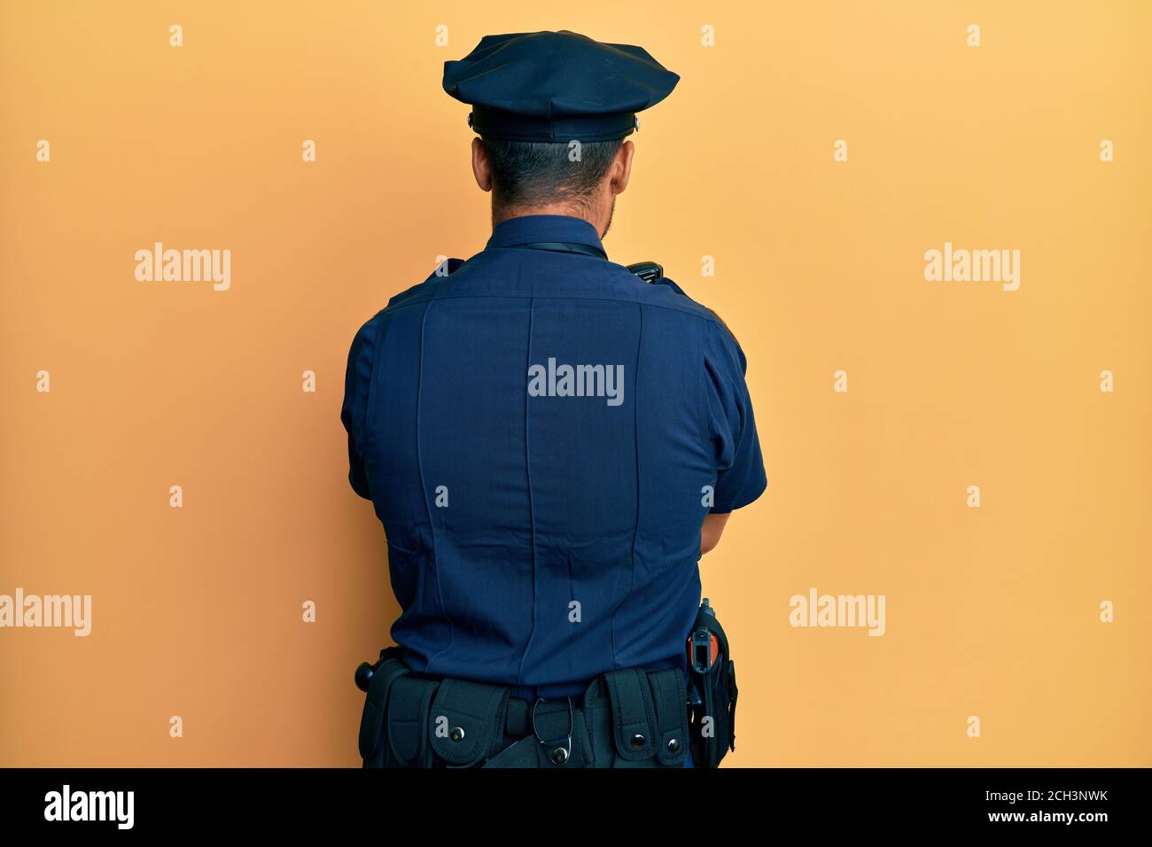 Handsome hispanic man wearing police uniform standing backwards looking ...