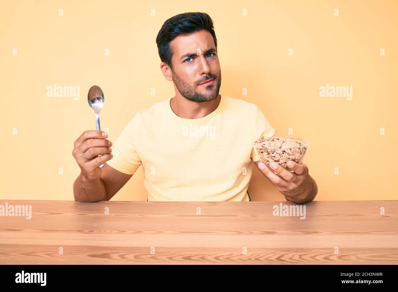 Young handsome hispanic man eating healthy whole grain celears sitting ...