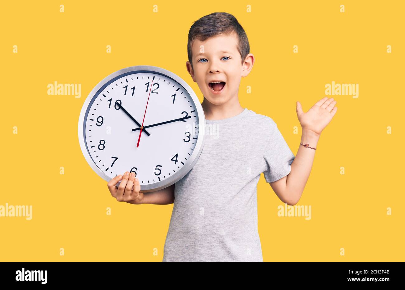 Cute blond kid holding big clock celebrating victory with happy smile ...