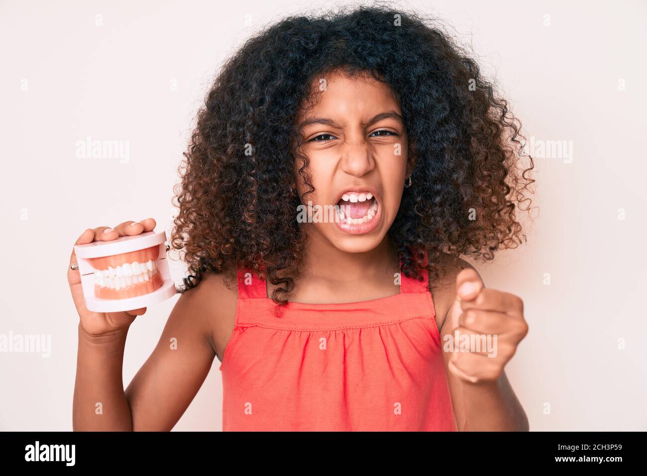 African american child with curly hair holding denture annoyed and ...