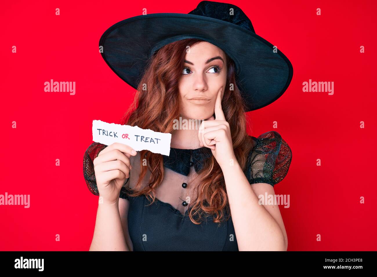 Young beautiful woman wearing witch halloween costume holding paper ...