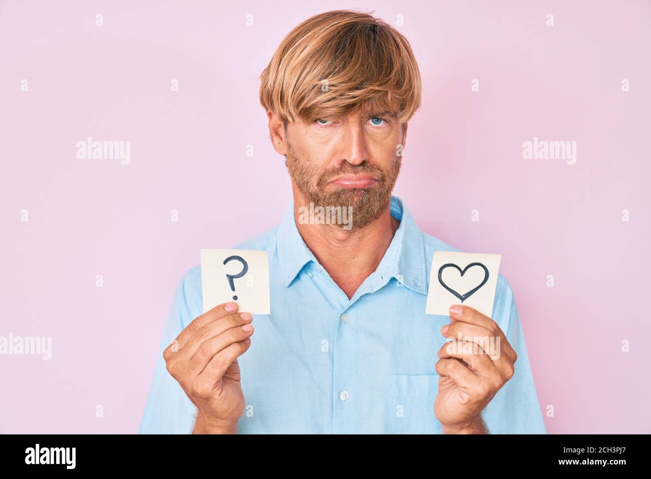 Young blond man holding heart and question mark reminder depressed and ...