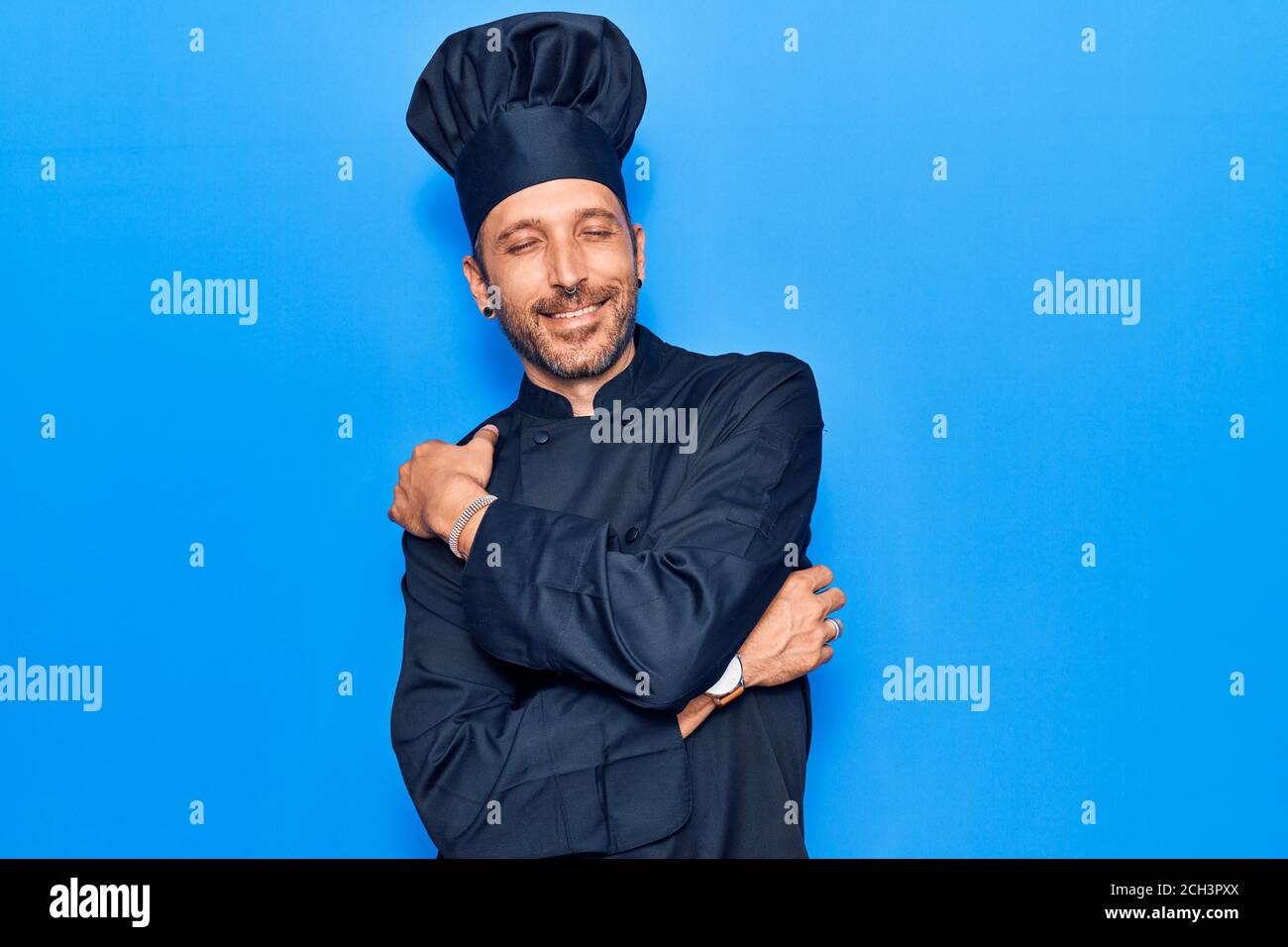 Young handsome man wearing cooker uniform hugging oneself happy and ...