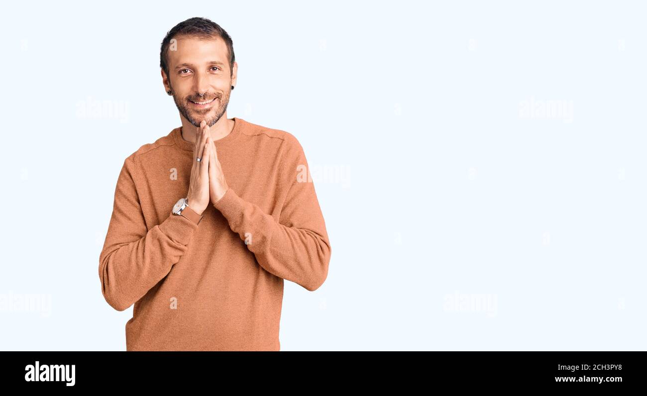 Young handsome man wearing casual clothes praying with hands together ...
