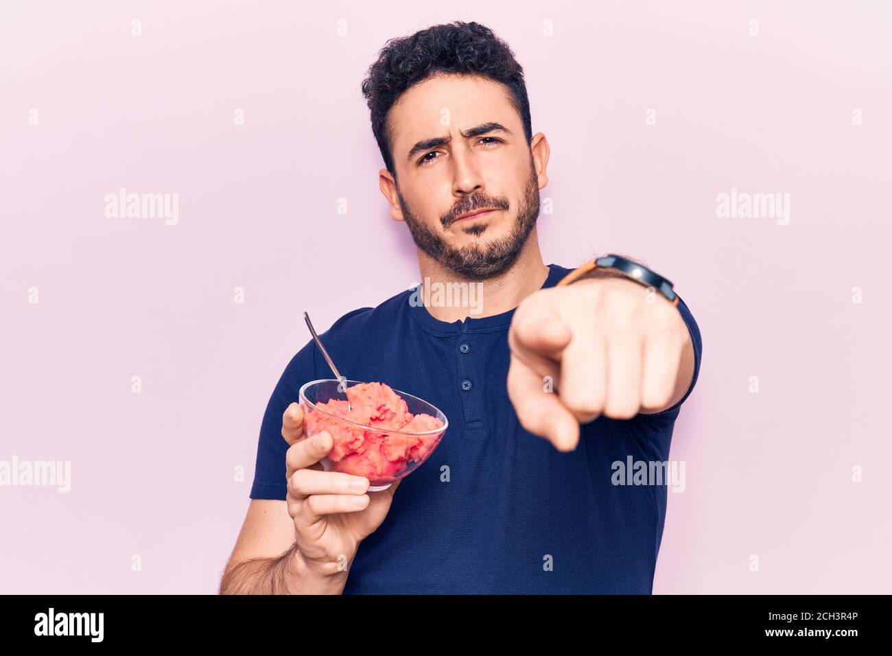 Young hispanic man holding ice cream pointing with finger to the camera ...