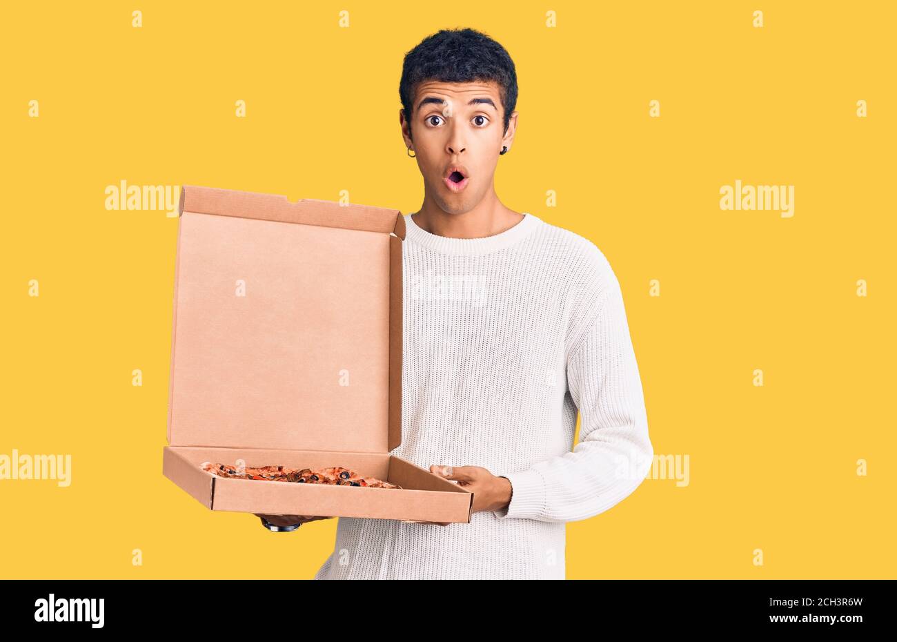 Young african amercian man holding delivery pizza box scared and amazed ...