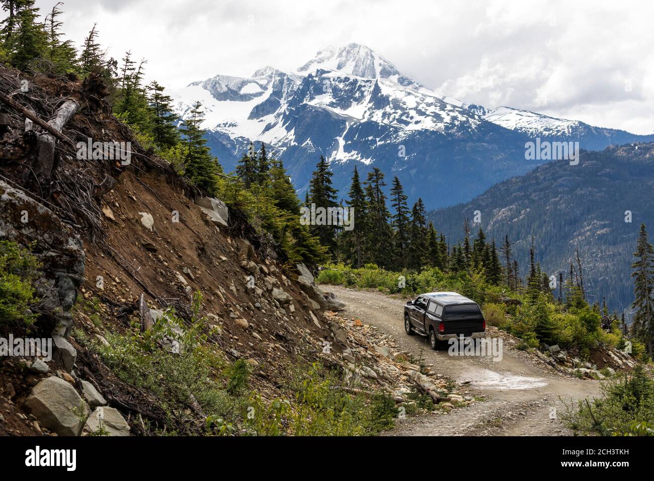 Modern vehicle driving along curvy logging road near rough slope during ...